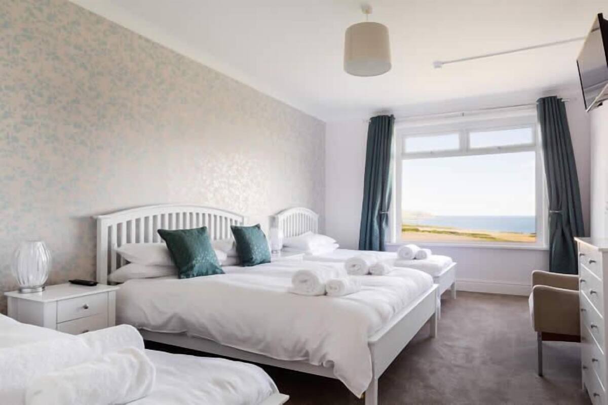 Quarto de hotel com uma cama grande, uma mesa de cabeceira, uma cadeira e vista para o mar.