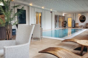 Uma área moderna de piscina interna com piso ladrilhado, espreguiçadeiras e um quadro de cardápio na parede.