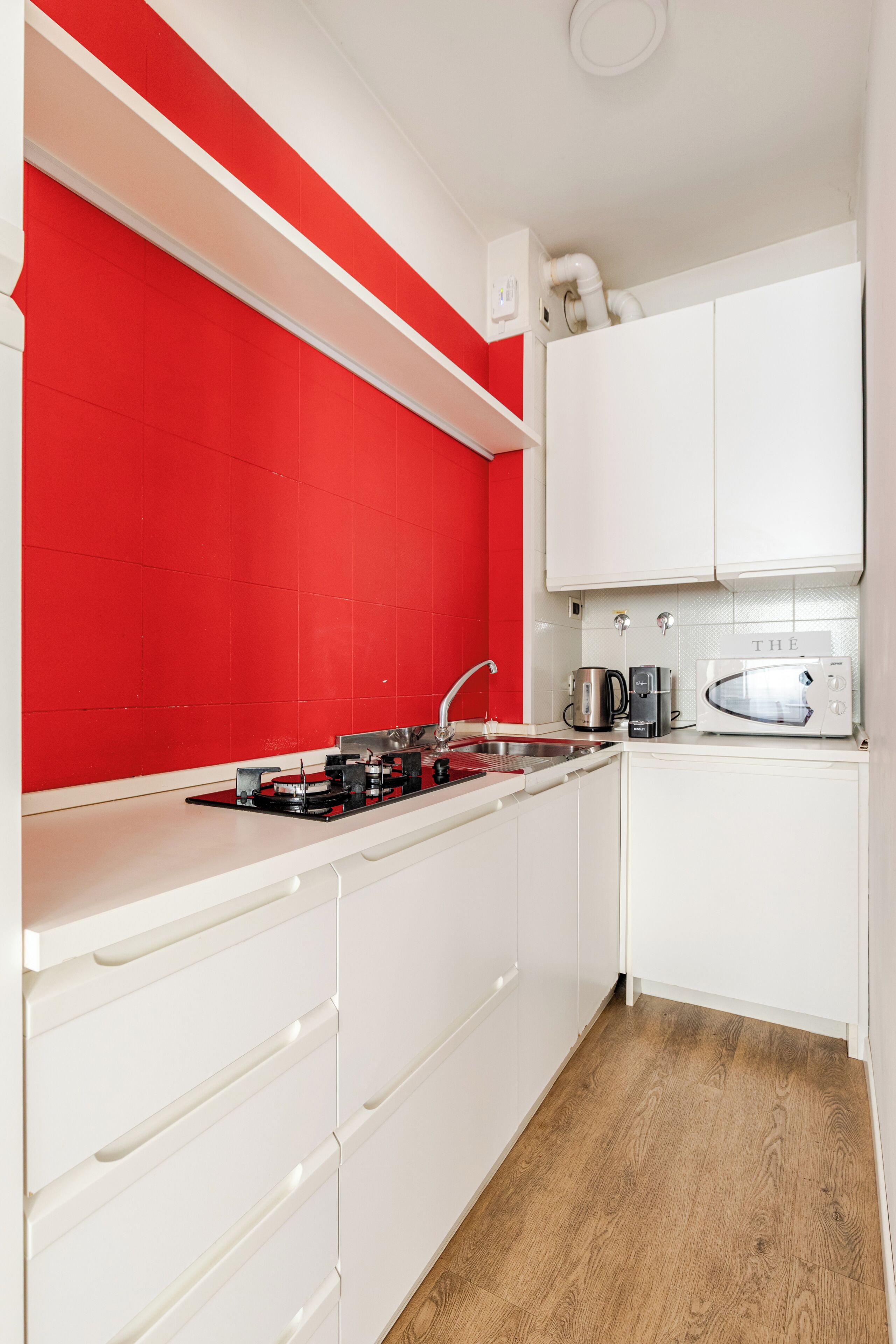 Cozinha com armários brancos, painel vermelho, micro-ondas, cafeteira e fogão a gás.