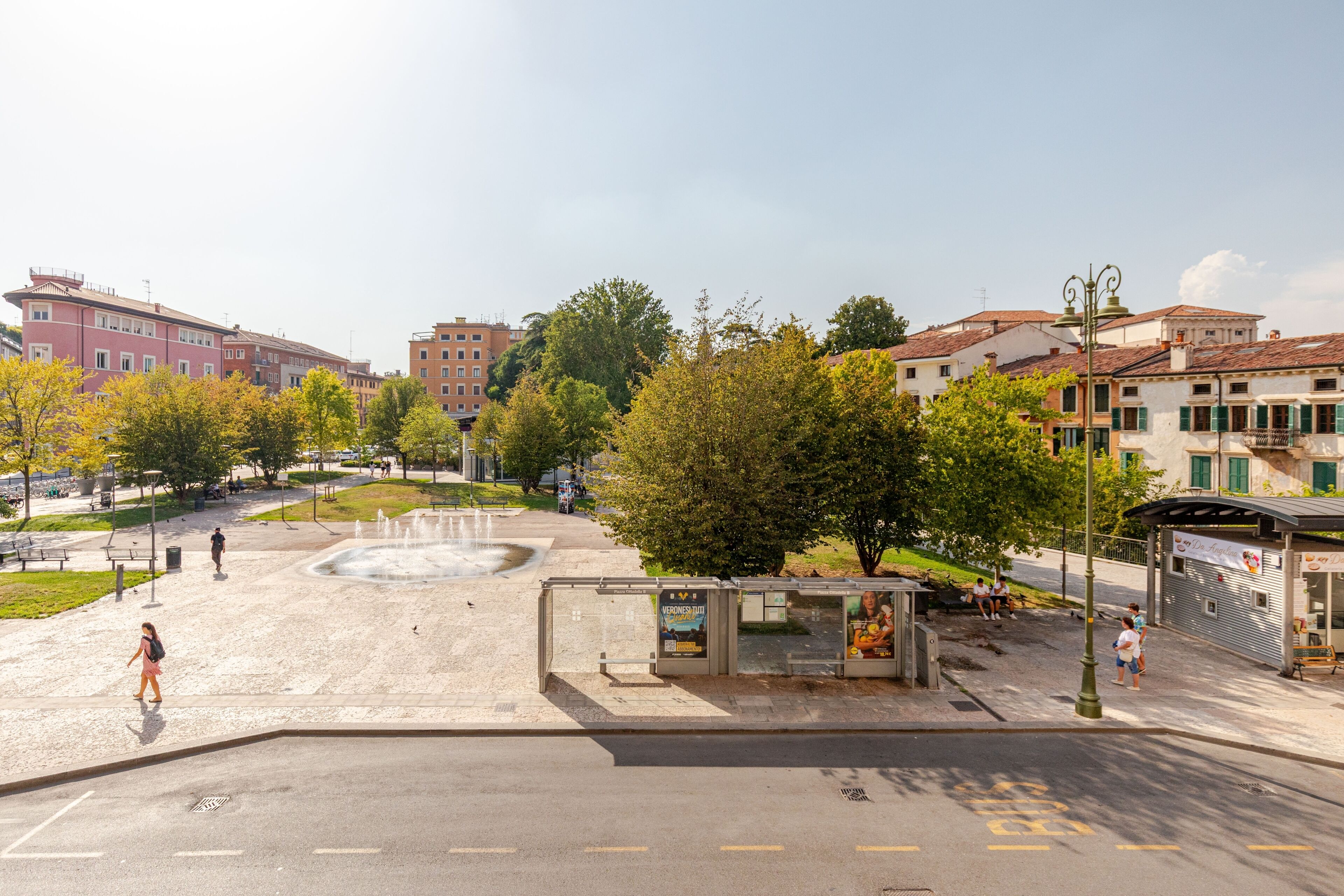 Uma praça pública com uma fonte, bancos e um ponto de ônibus.