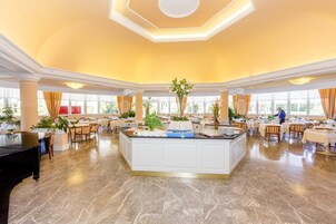 Um amplo hall de hotel com uma ilha central, diversas áreas de refeições e grandes janelas.