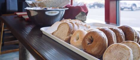 Uma bandeja de bagels e uma tigela de sopa sobre uma mesa de madeira em um quarto com uma janela grande.
