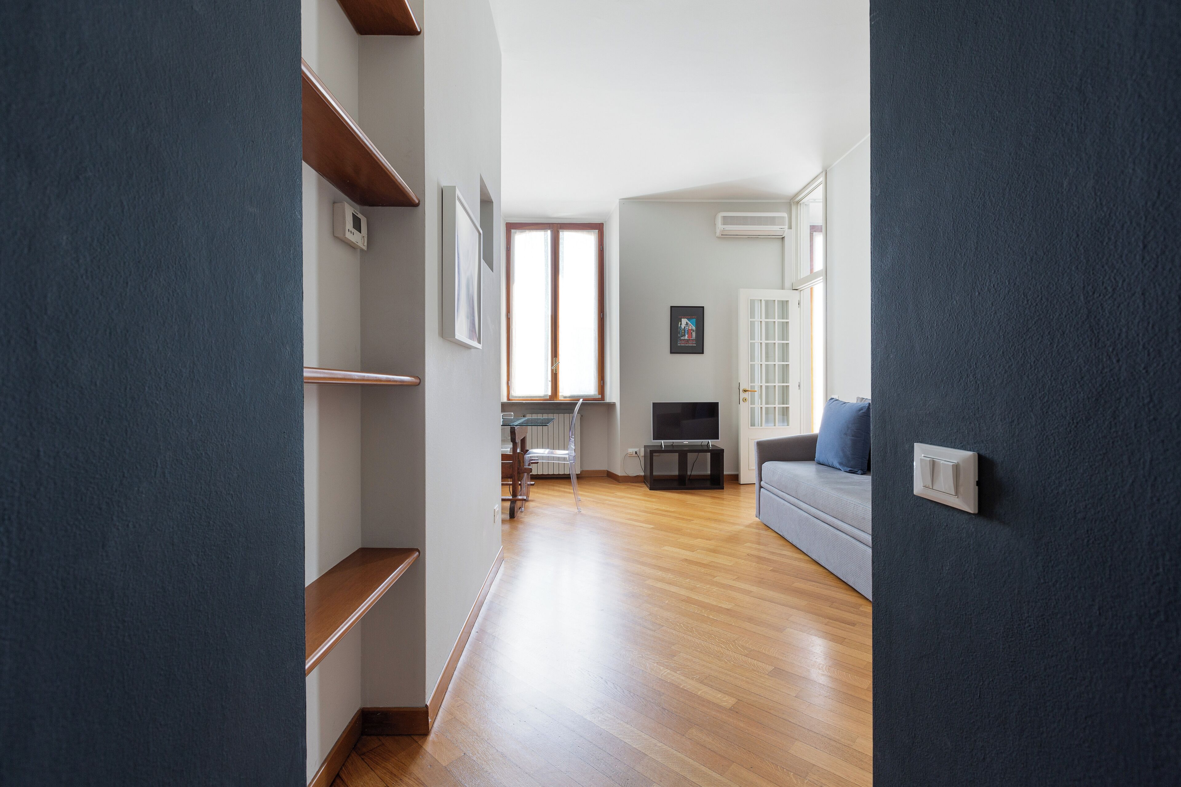 Uma sala de estar moderna com piso de madeira, um sofá cinza, uma televisão e um espaço de refeições com mesa e cadeiras.