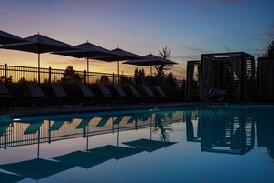 Área de piscina com espreguiçadeiras e guarda-sóis, uma cerca e uma estrutura de edifício.