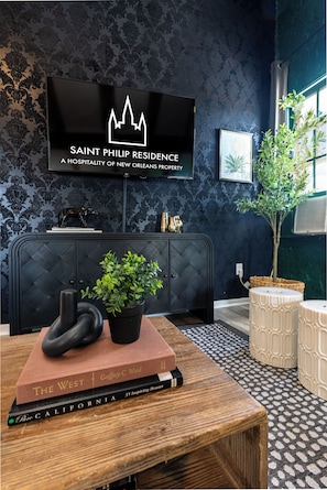 Uma sala de estar moderna com televisão de tela plana exibindo um logotipo, uma planta em vaso, livros e um vaso decorativo sobre uma mesa de centro de madeira.