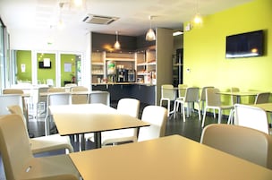 Um café moderno com mesas e cadeiras brancas, um balcão com máquina de café e uma TV na parede.