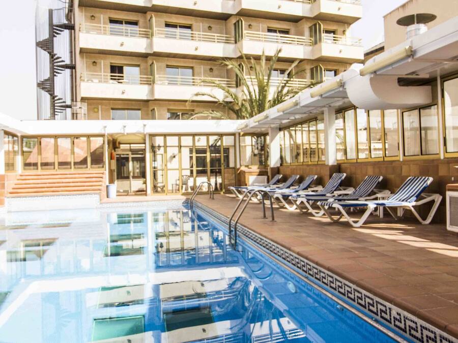 Uma piscina com espreguiçadeiras, um edifício com varandas e um céu limpo.