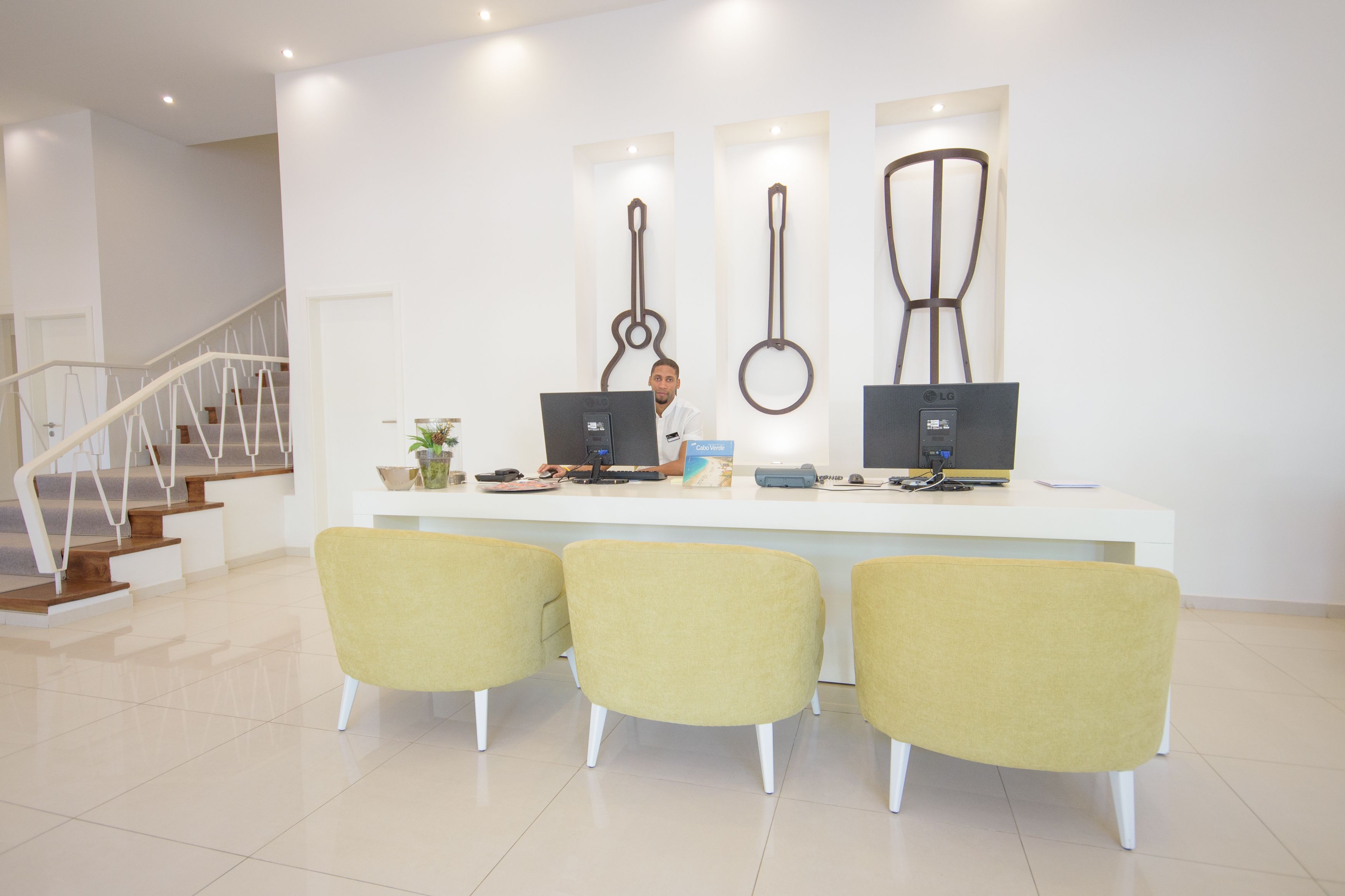Um espaço de escritório moderno com uma mesa branca, dois computadores e três cadeiras amarelas.