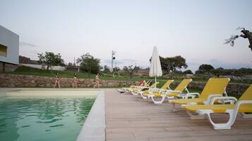 Área de piscina com espreguiçadeiras e um muro de pedra.