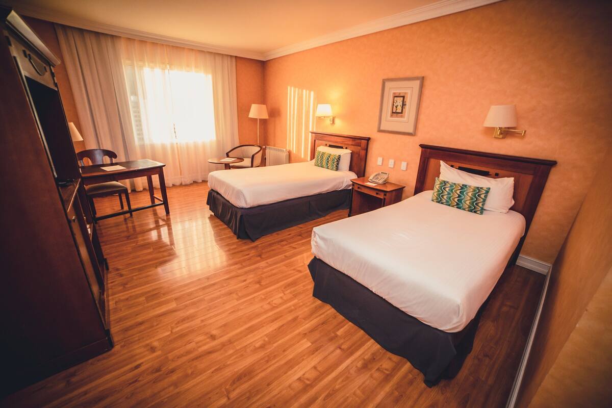 Quarto de hotel com duas camas, uma escrivaninha e uma cadeira.