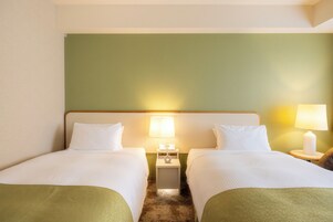 Quarto de hotel com duas camas, uma mesa de cabeceira com abajur e uma parede verde decorativa.