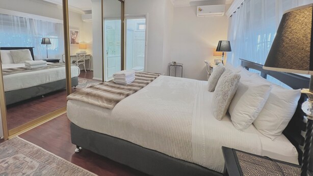 Quarto de hotel moderno com uma cama grande, área de estar, escrivaninha, espelho e janela com cortinas.