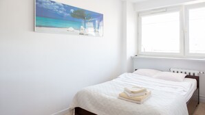 Um quarto com uma cama, um quadro de uma praia e uma janela com vista para o céu.