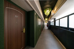Um corredor com uma porta de madeira identificada como '501', paredes verdes e um teto com plantas pendentes.