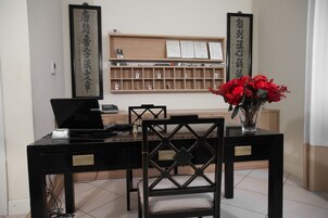 Quarto com uma escrivaninha, cadeiras, um laptop, um vaso com flores e estantes com diplomas emoldurados.