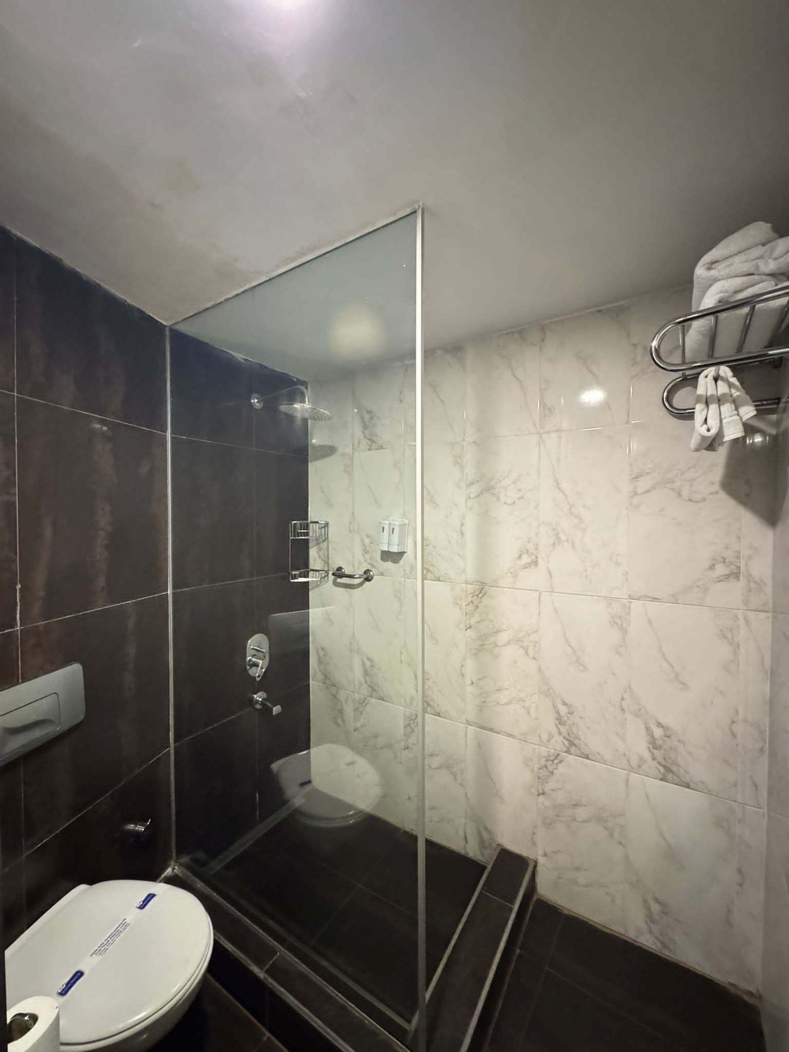 Um banheiro moderno com box de vidro, vaso sanitário e porta-toalhas.