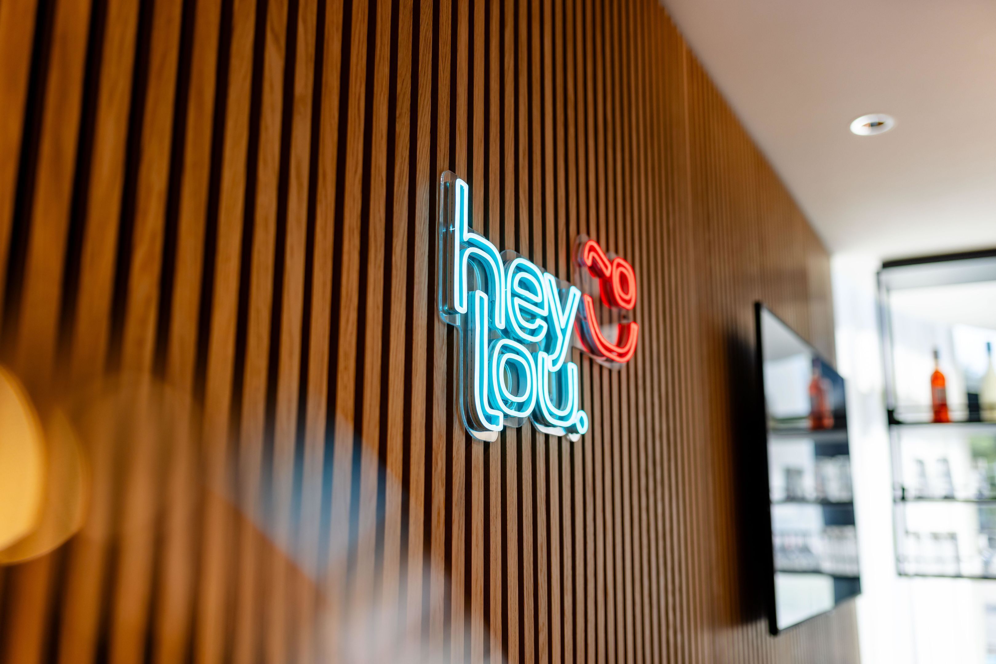 Um letreiro de neon com o texto 'hey you' em uma parede de madeira.