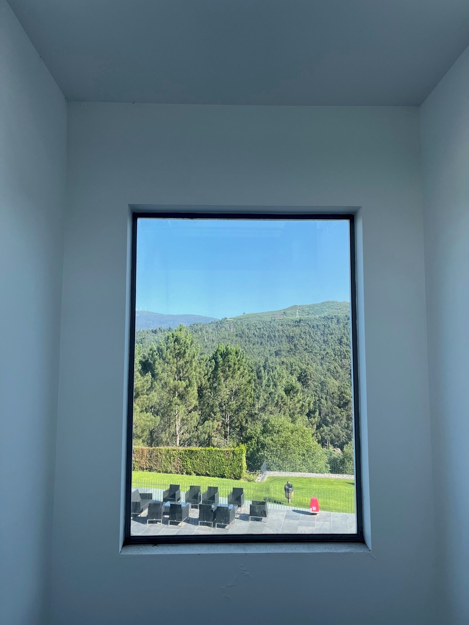 Quarto com uma janela grande com vista para uma paisagem verde com árvores e colinas.