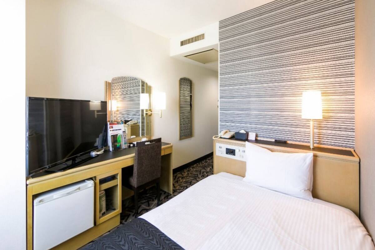 Quarto de hotel com cama, escrivaninha, televisão, telefone e minibar.