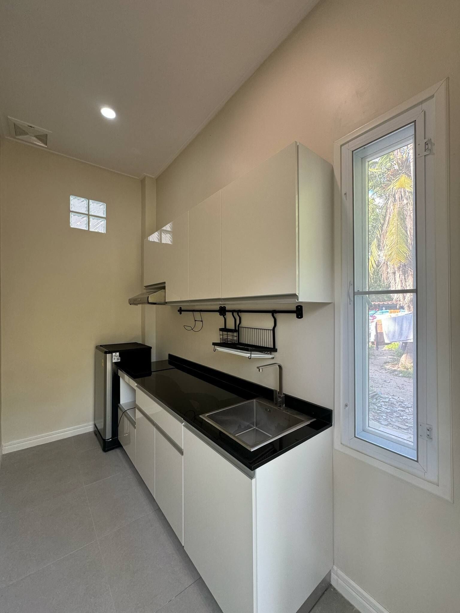 Uma cozinha compacta com armários brancos, bancada preta e janela com vista para o verde.