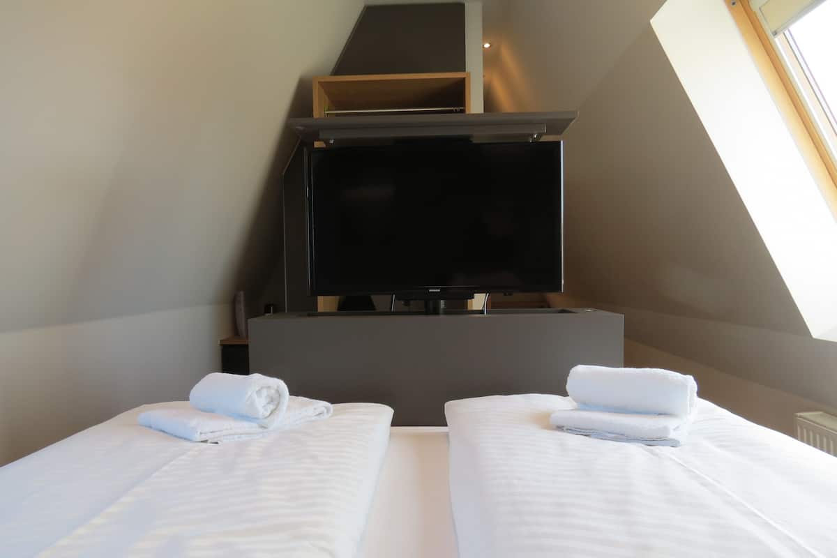 Quarto de hotel com duas camas, uma televisão de tela plana na parede e um claraboia.
