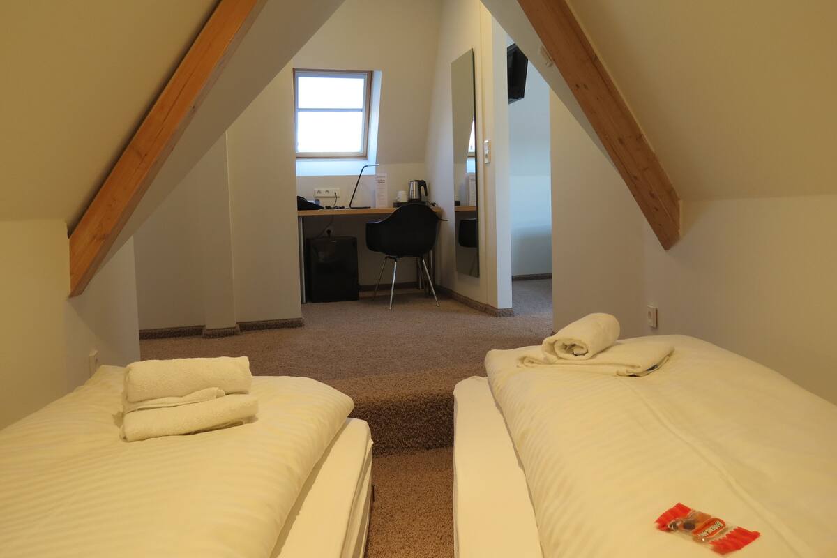 Quarto com duas camas, uma escrivaninha e uma cadeira.