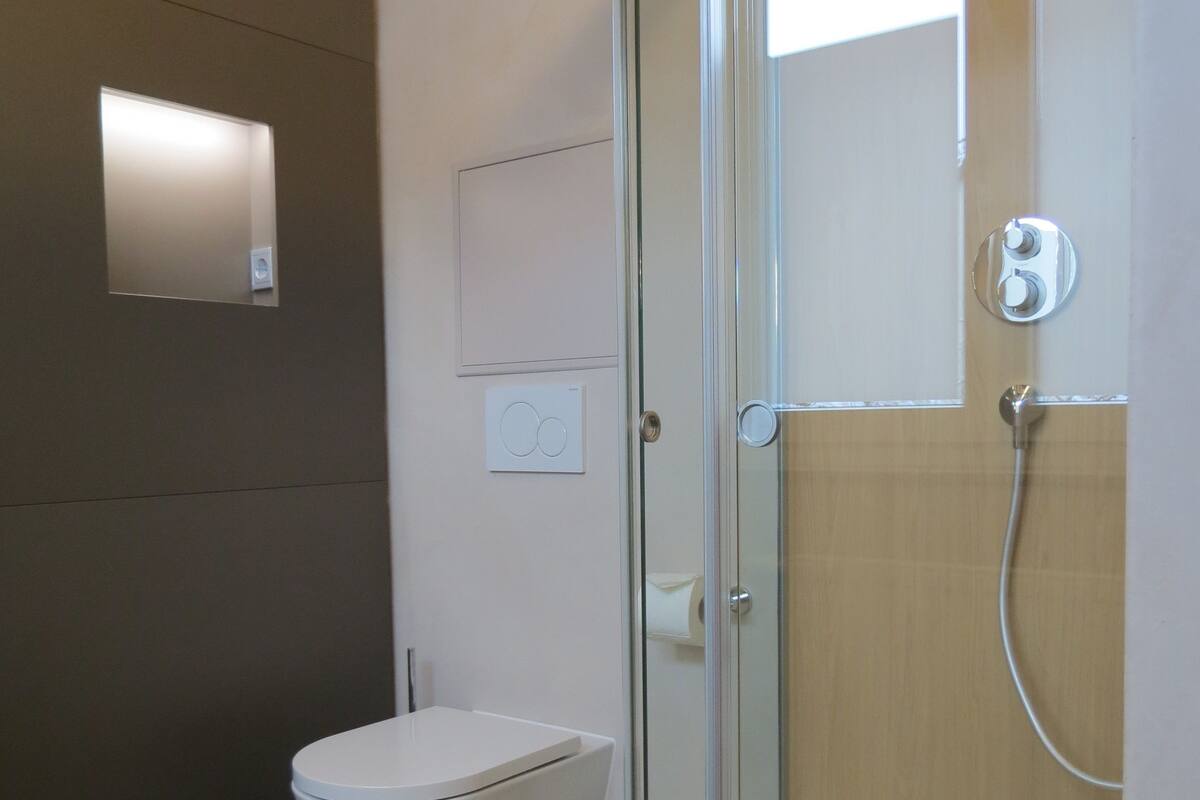 Um banheiro moderno com box de vidro, vaso sanitário branco e dispensador de toalhas fixado na parede.