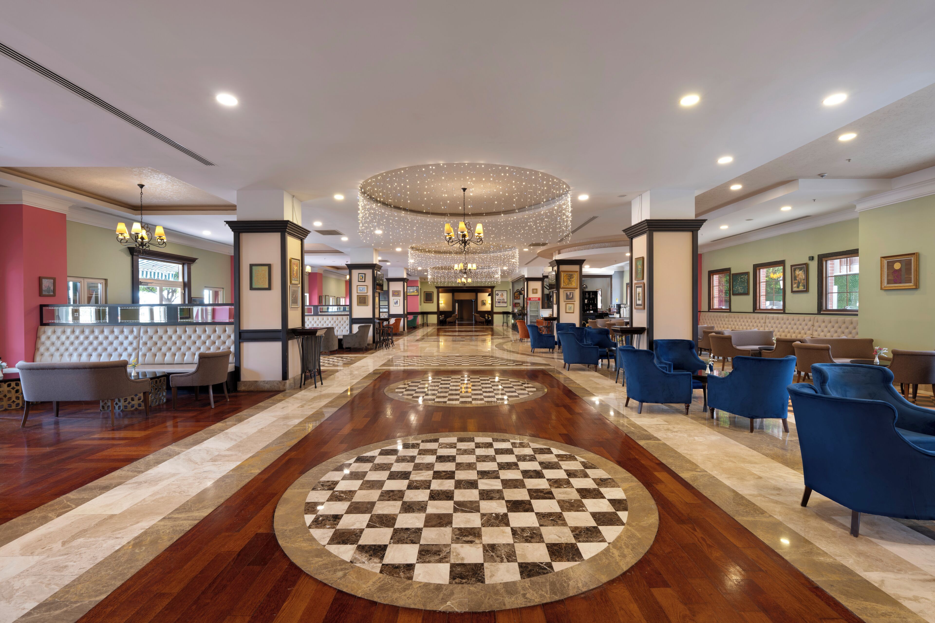Um hall de hotel com piso xadrez, áreas de estar, lustres e obras de arte emolduradas nas paredes.