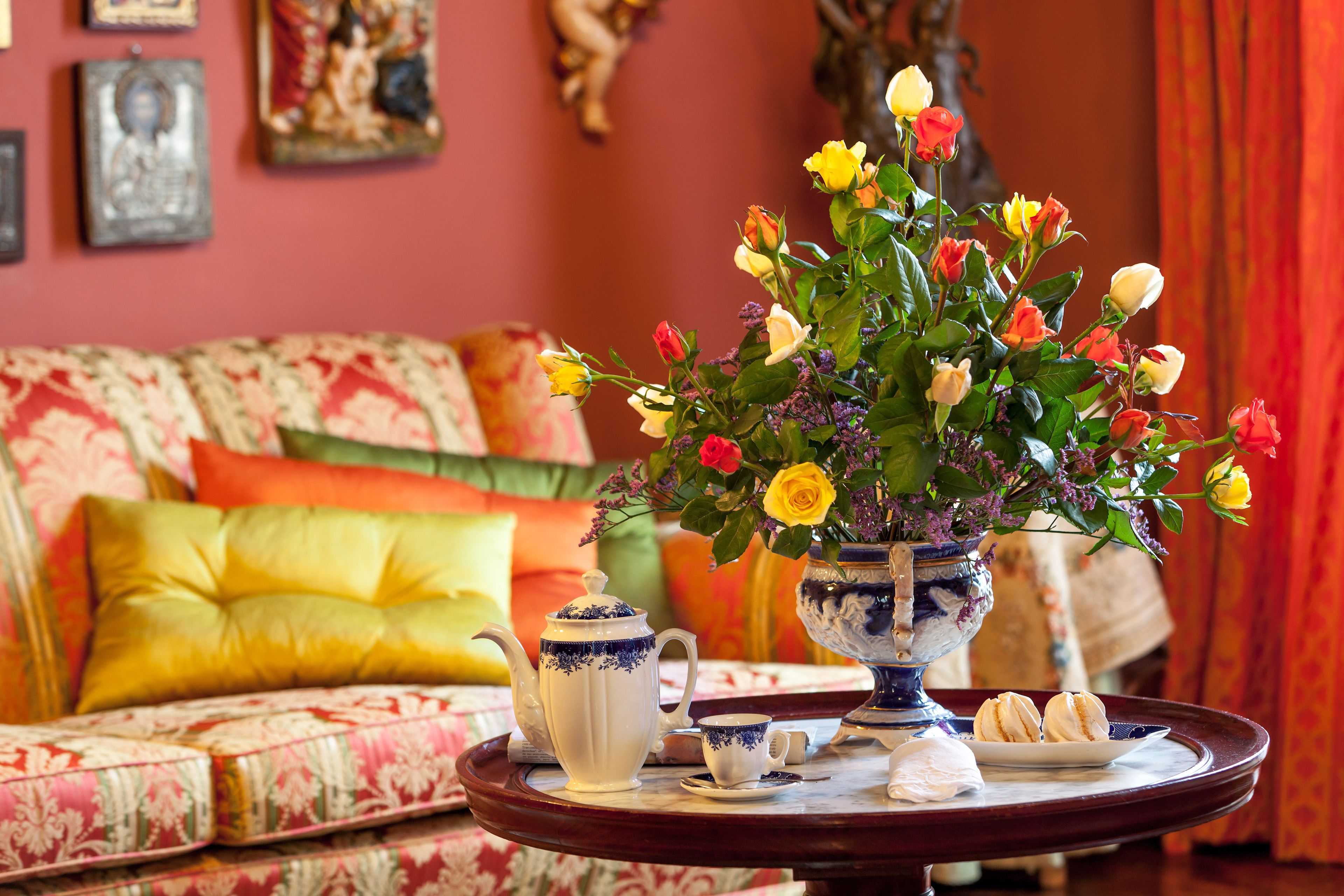 Uma sala de estar com um arranjo floral, um sofá, almofadas e uma bandeja com xícaras de chá e doces.