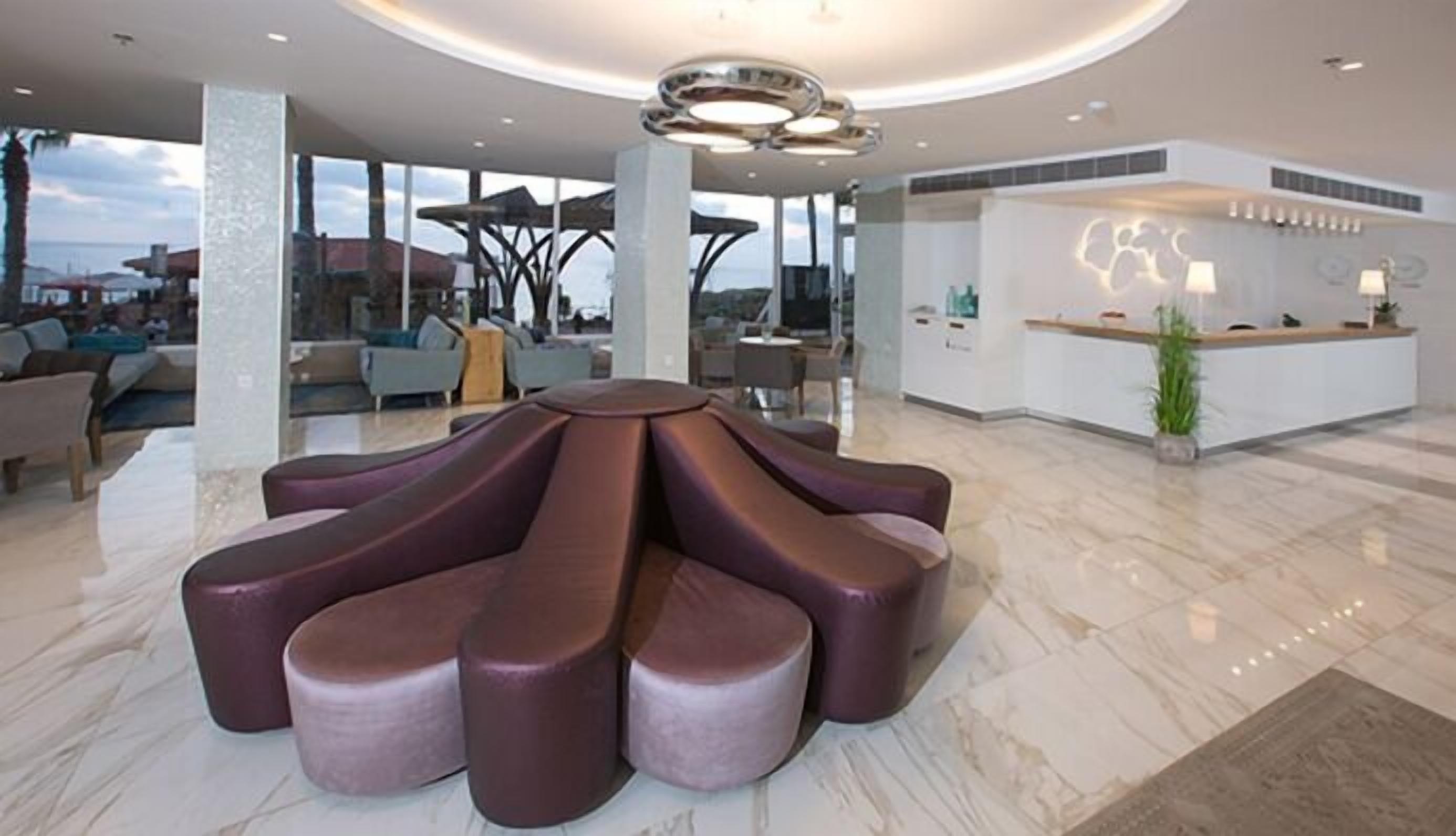 Um hall moderno com área de estar central, balcão de recepção e vista para o exterior.