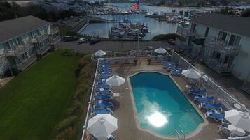 Piscina com espreguiçadeiras e guarda-sóis, cercada por uma grade, com um porto e barcos ao fundo.