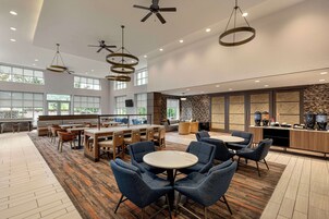 Um hall de hotel espaçoso, com pé-direito alto, várias áreas de estar e um bar central.