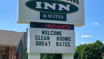 Placa de hotel com o nome 'Green Gables Inn & Suites' e a mensagem 'SEM QUARTOS' e 'BEM-VINDOS, QUARTOS LIMPOS, ÓTIMAS TAXAS'.