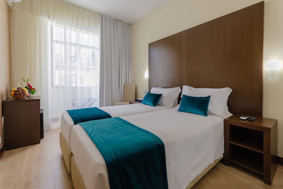 Quarto de hotel com duas camas, cabeceira de madeira, mesa de cabeceira com um controle remoto e escrivaninha com um vaso de flores.