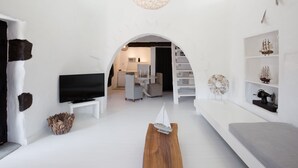 Uma sala de estar moderna com uma televisão de tela plana, uma mesa de centro de madeira e uma pequena réplica de veleiro.