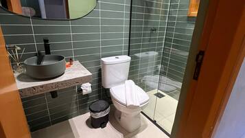 Casa de banho com sanita, lavatório e zona de duche separada por vidro.