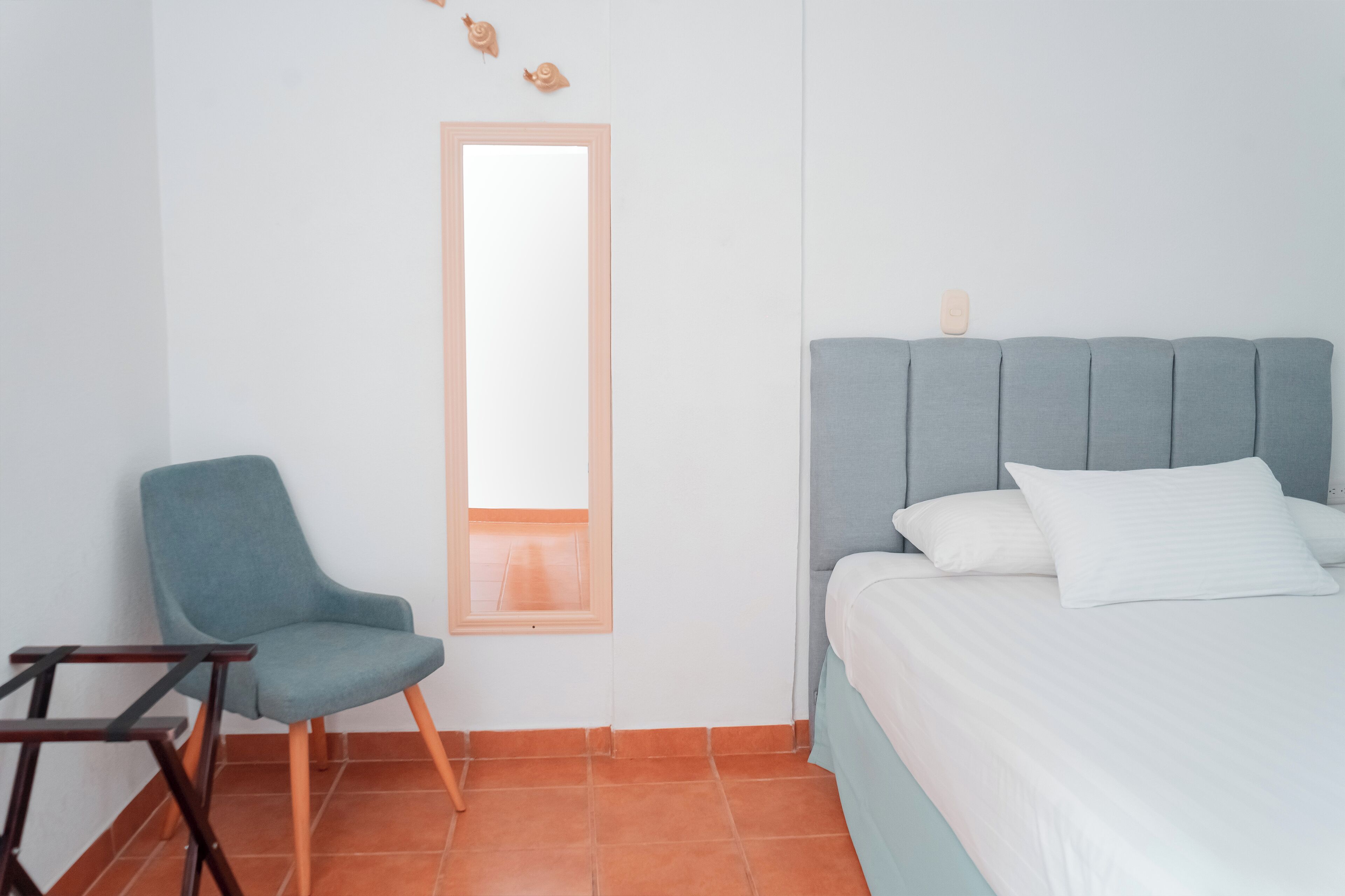 Quarto com cama, cadeira, janela e luminária fixada na parede.