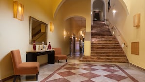 Um hall amplo com piso xadrez, escada e área de estar com cadeiras e mesa.