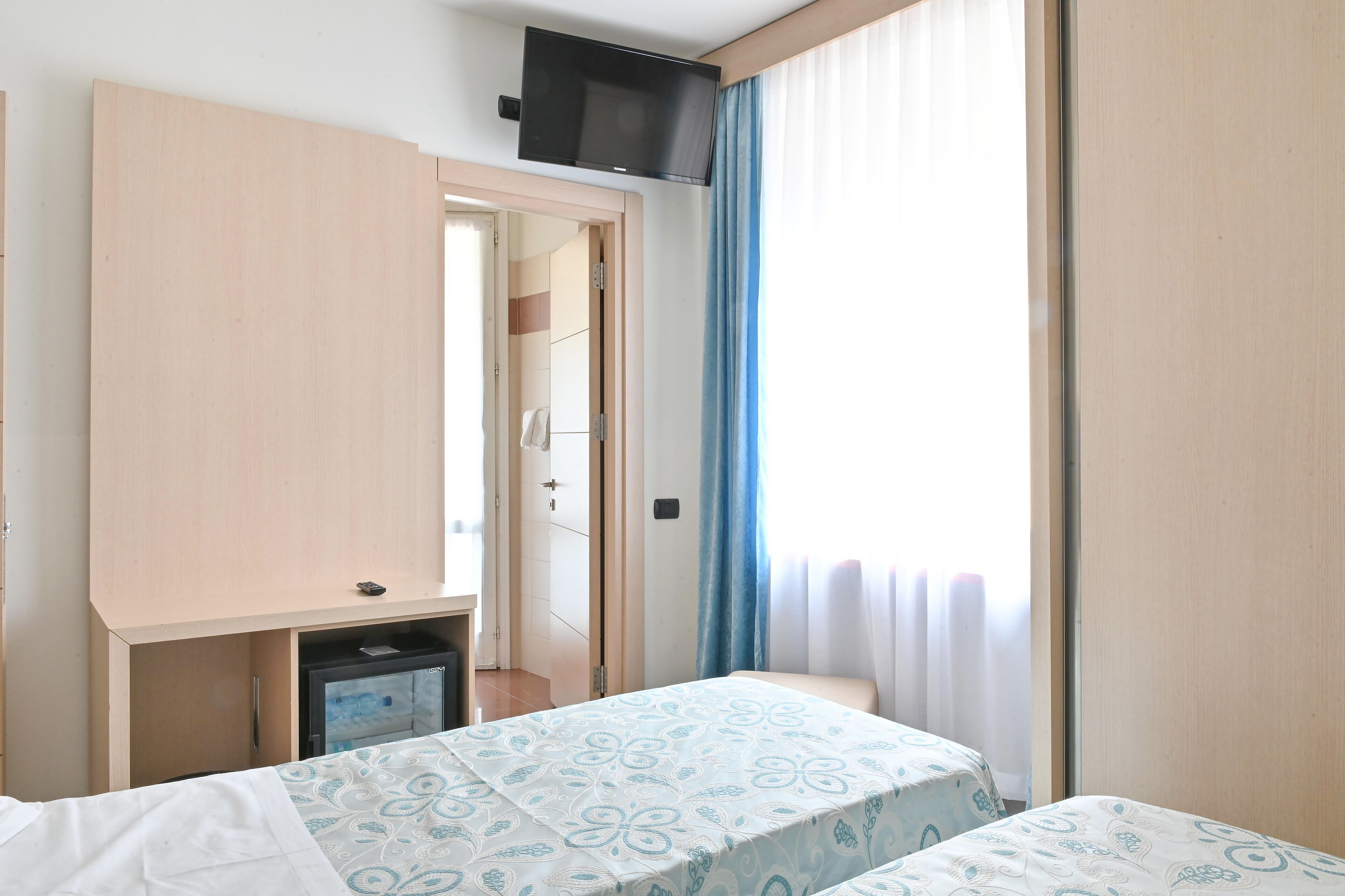 Quarto de hotel com cama, escrivaninha, televisão e guarda-roupa.
