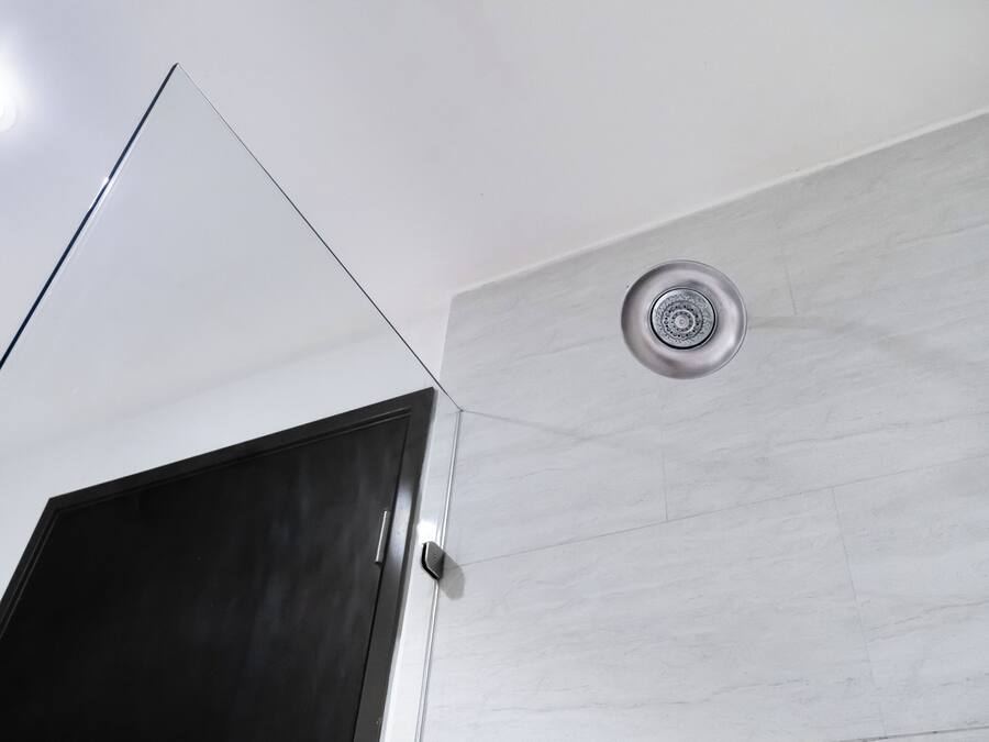 Uma casa de banho moderna com parede revestida a azulejos brancos, porta preta e luminária no teto.