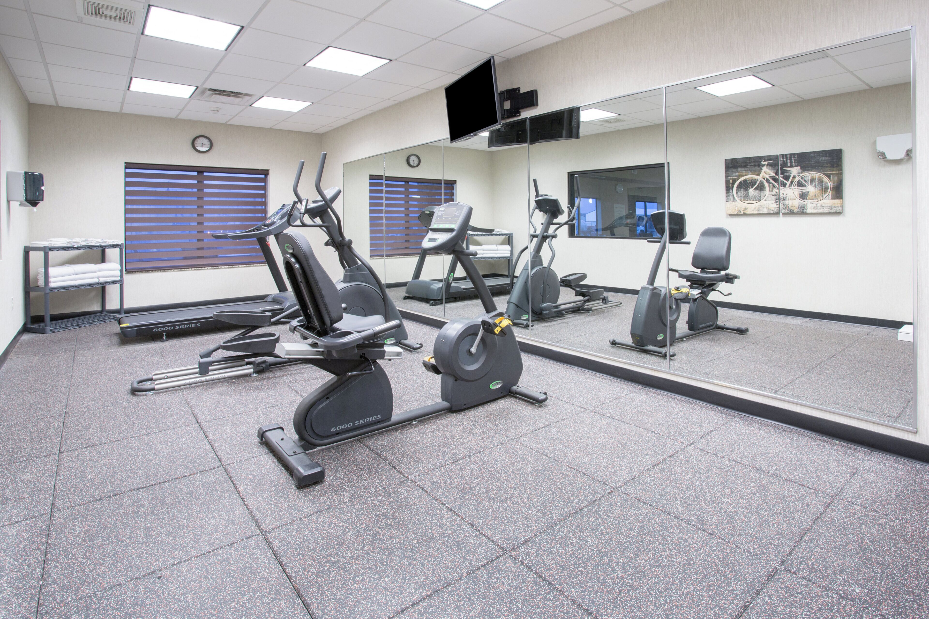 Uma academia com diversos equipamentos de exercícios, um painel de espelhos e um relógio na parede.