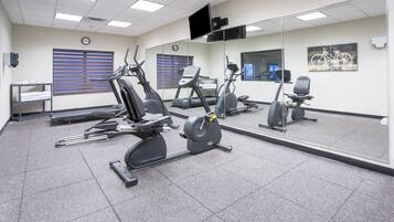 Uma academia com diversos equipamentos de exercícios, um painel de espelhos e um relógio na parede.