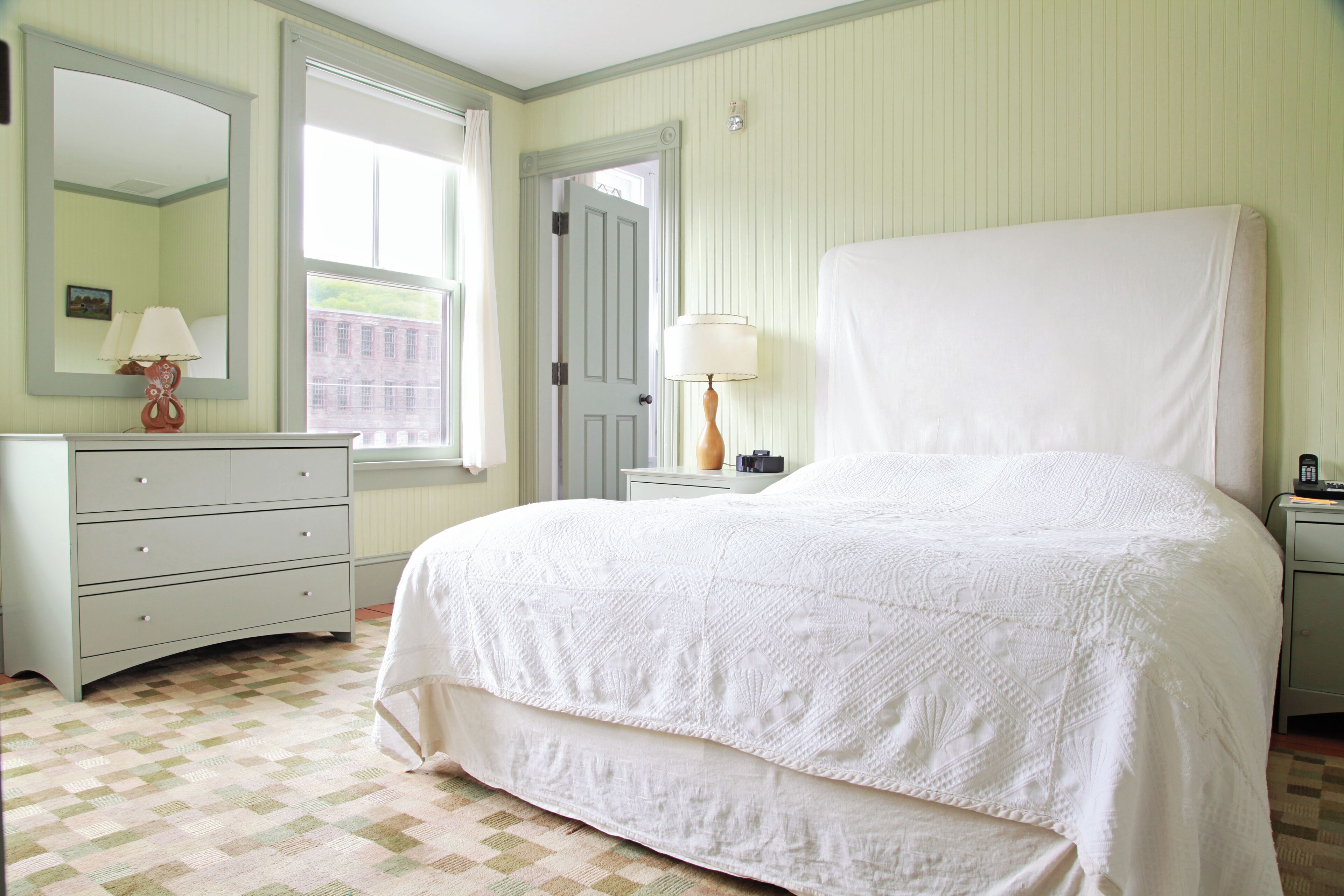 Quarto com cama grande, cômoda, espelho e janela com cortinas.