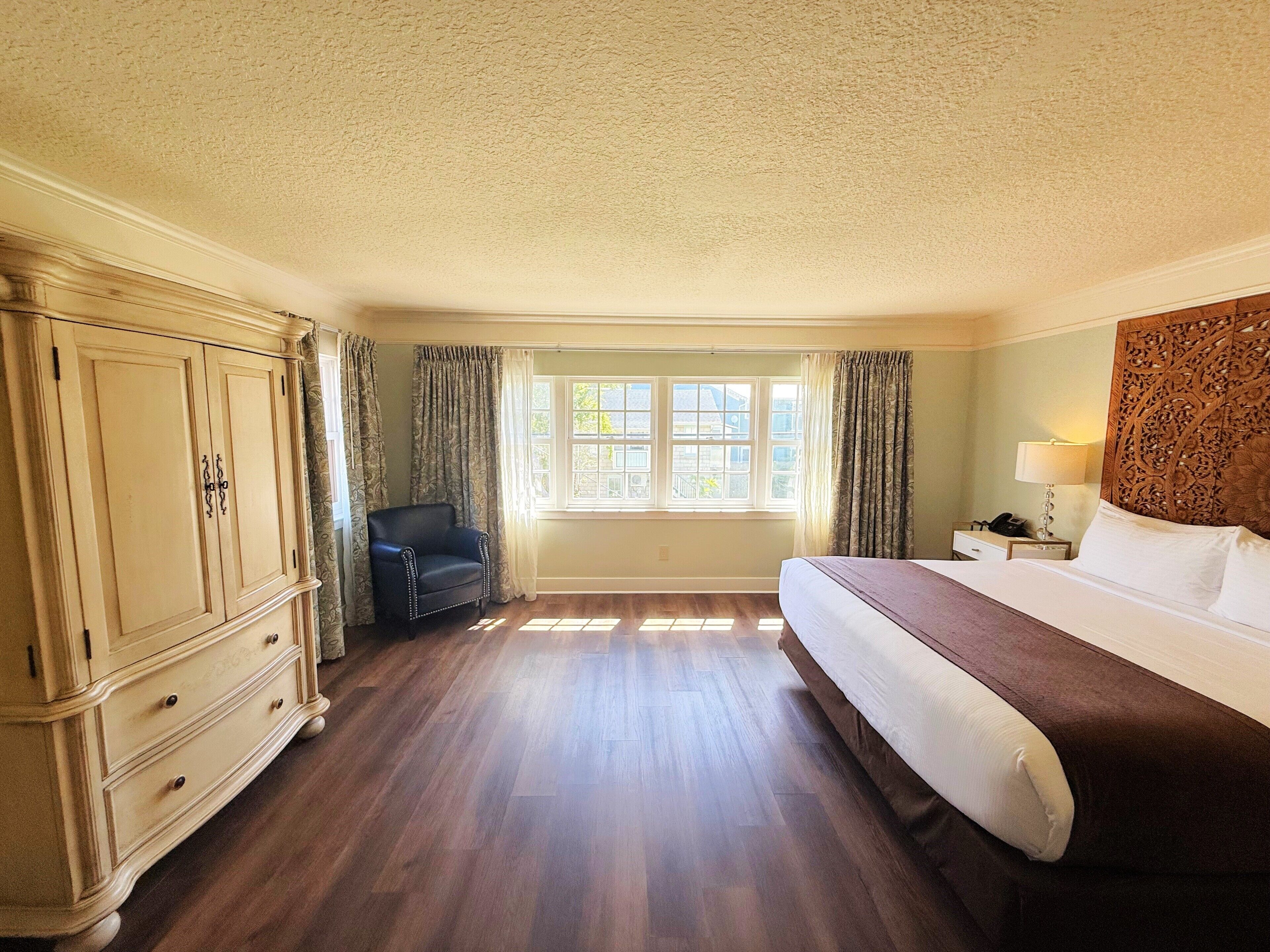 Quarto de hotel com uma cama grande, um guarda-roupa, uma cadeira e uma janela com cortinas.