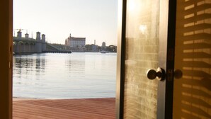 Uma porta dá para uma varanda com vista para águas calmas e um horizonte urbano ao fundo.