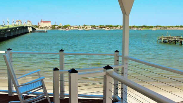 Um calçadão à beira-mar com guarda-corpo branco, um banco e vista para o horizonte urbano.