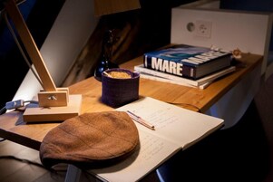 Uma escrivaninha com um caderno, caneta, um pequeno recipiente, uma luminária e um livro intitulado 'Mare'.