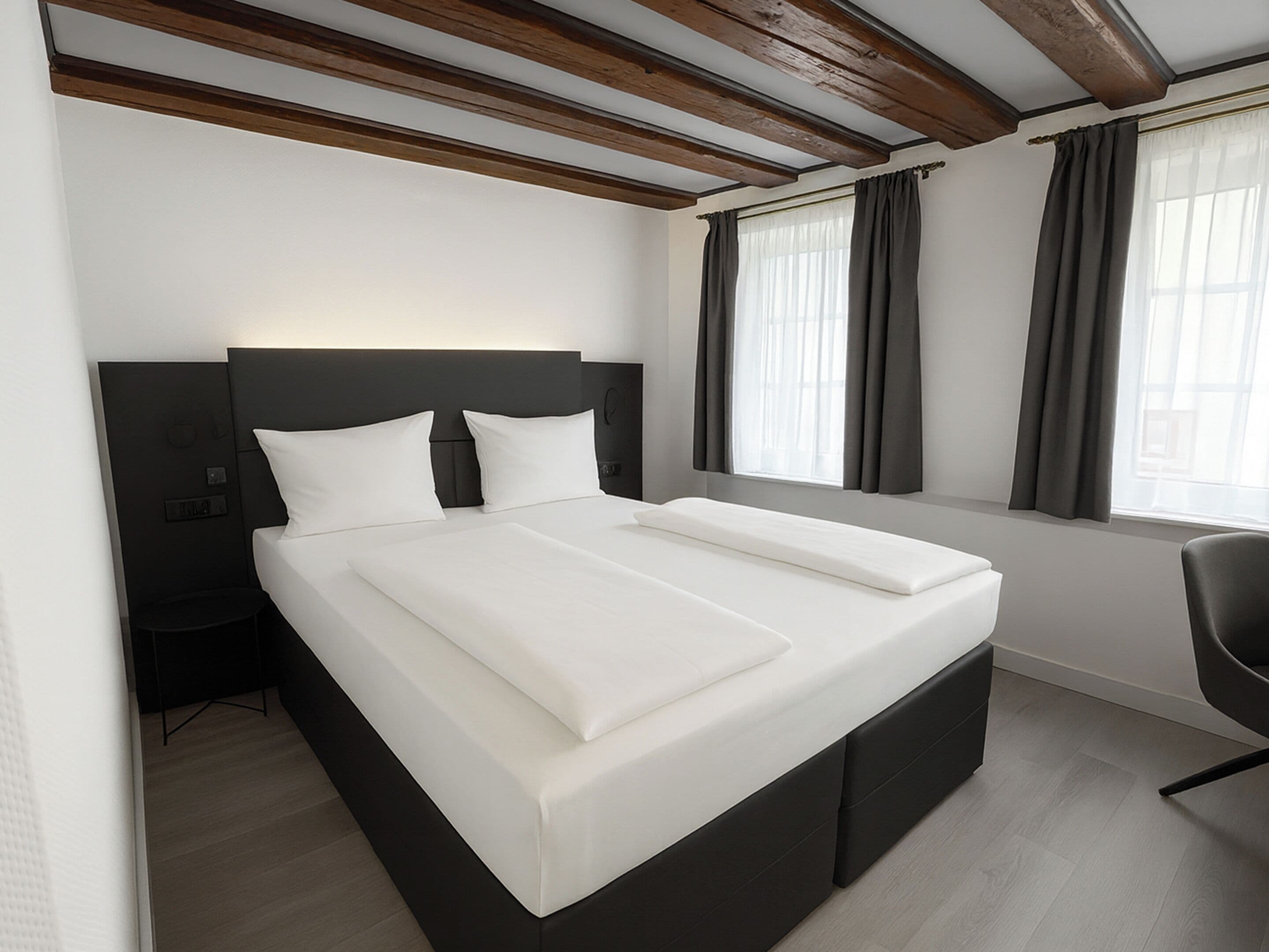 Quarto moderno com uma cama grande, cabeceira escura e teto de madeira.