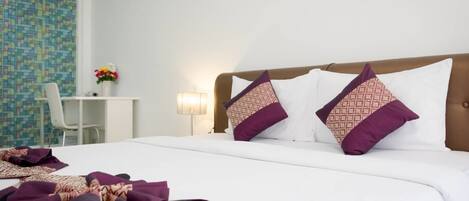 Quarto de hotel com uma cama, duas almofadas estampadas, uma mesa de cabeceira com abajur, uma cadeira e uma parede com padrão geométrico.