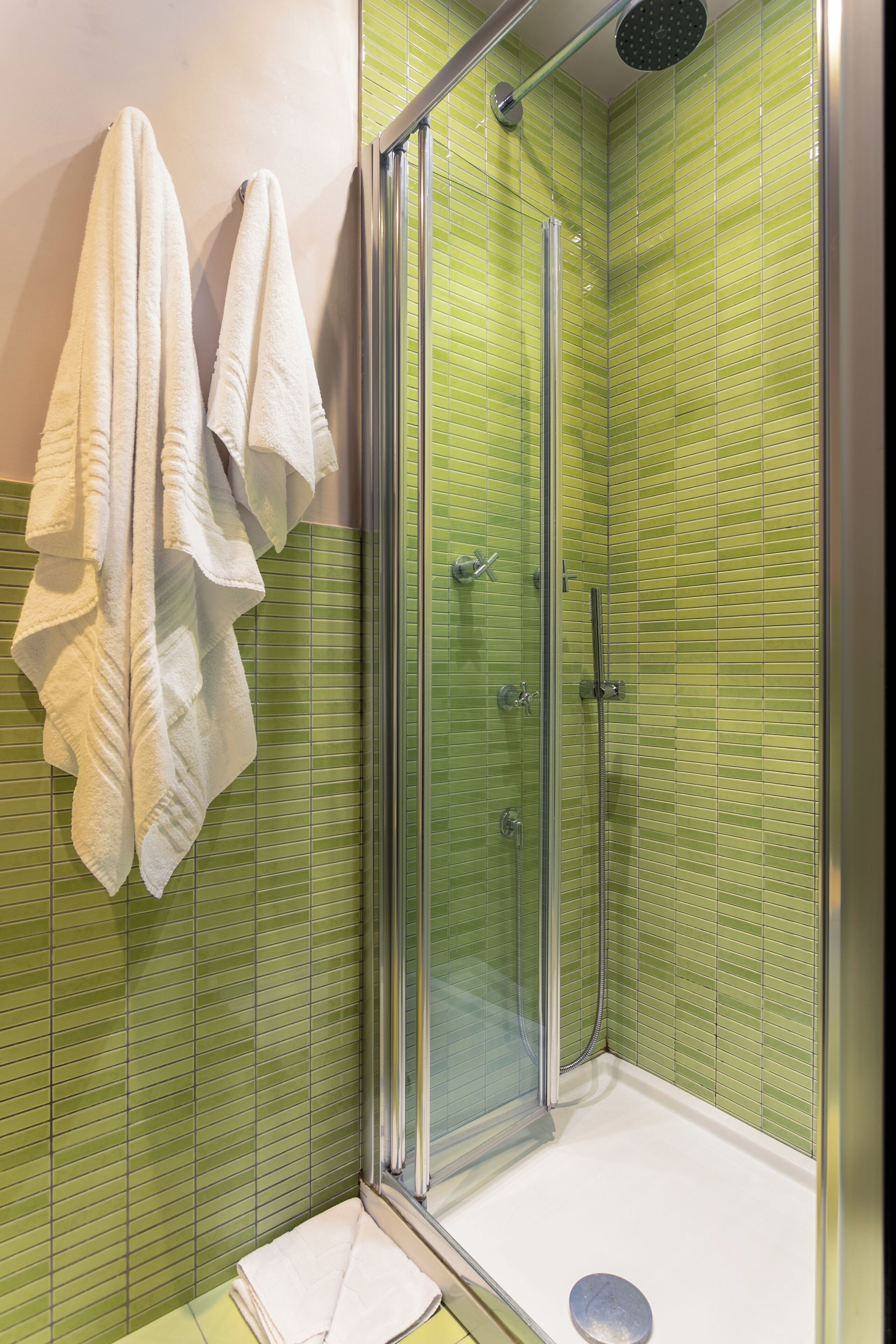 Chuveiro com porta de vidro e parede revestida de azulejos verdes.